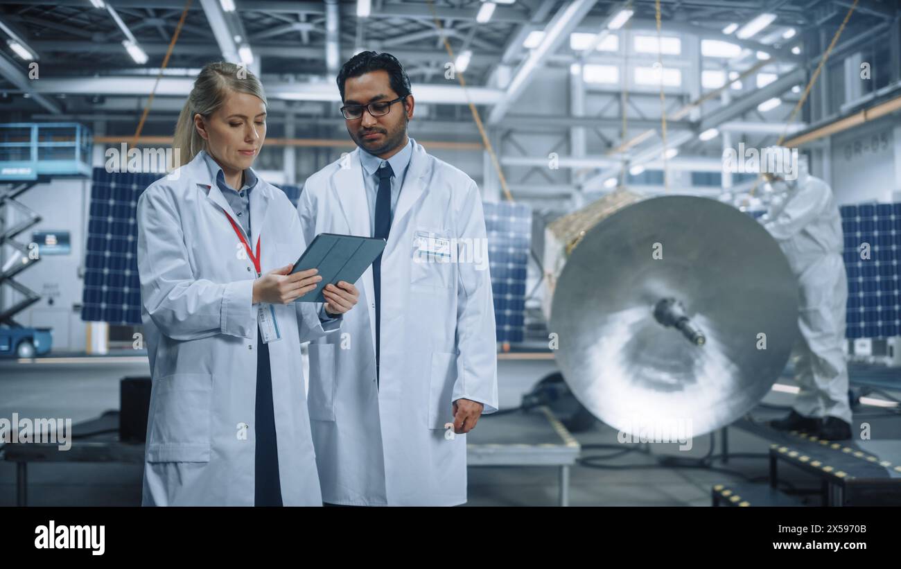 Two Engineers Talk, Use Tablet Computer while Working on Satellite ...