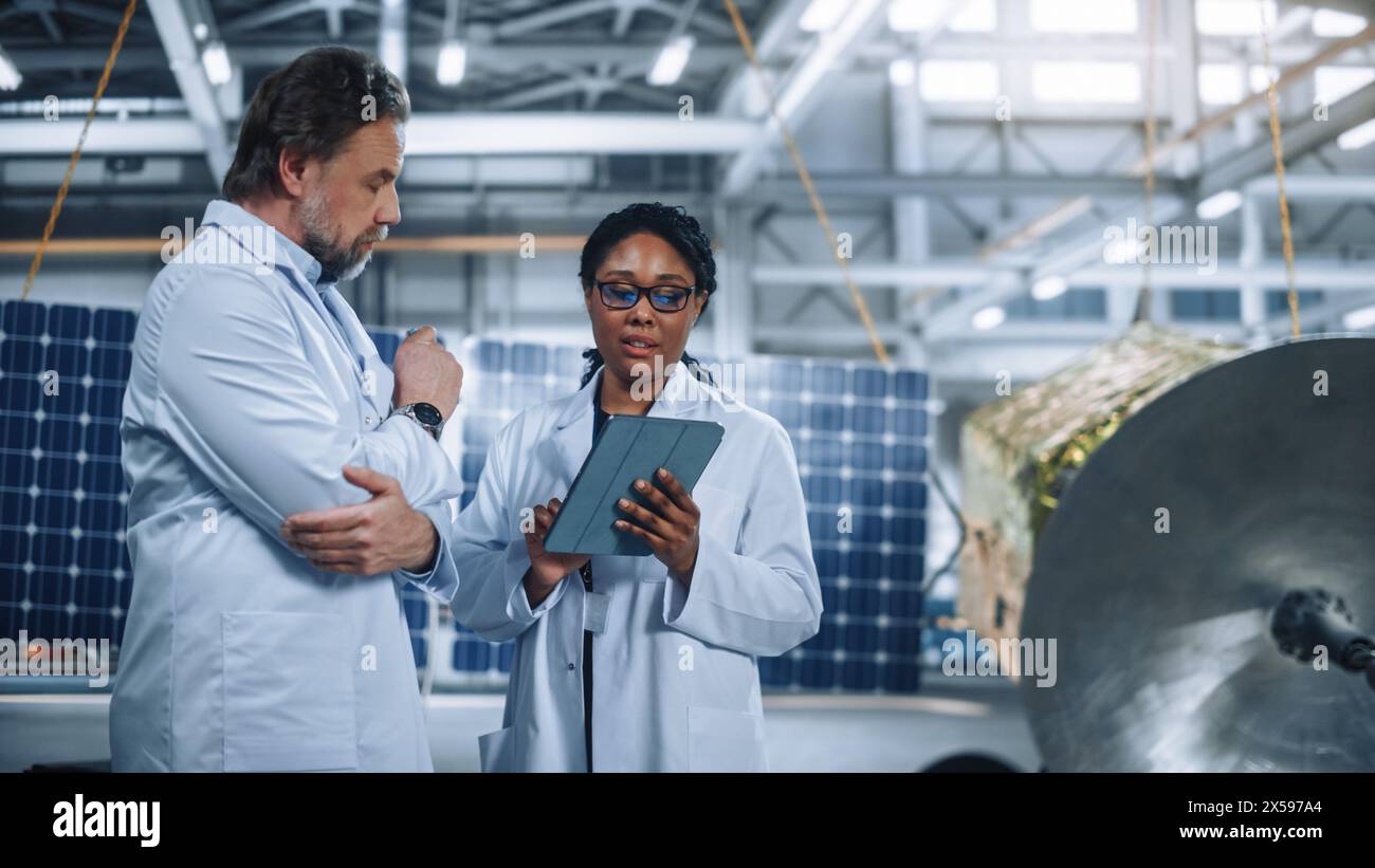 Two Engineers Talk, Use Tablet Computer while Working on Satellite ...