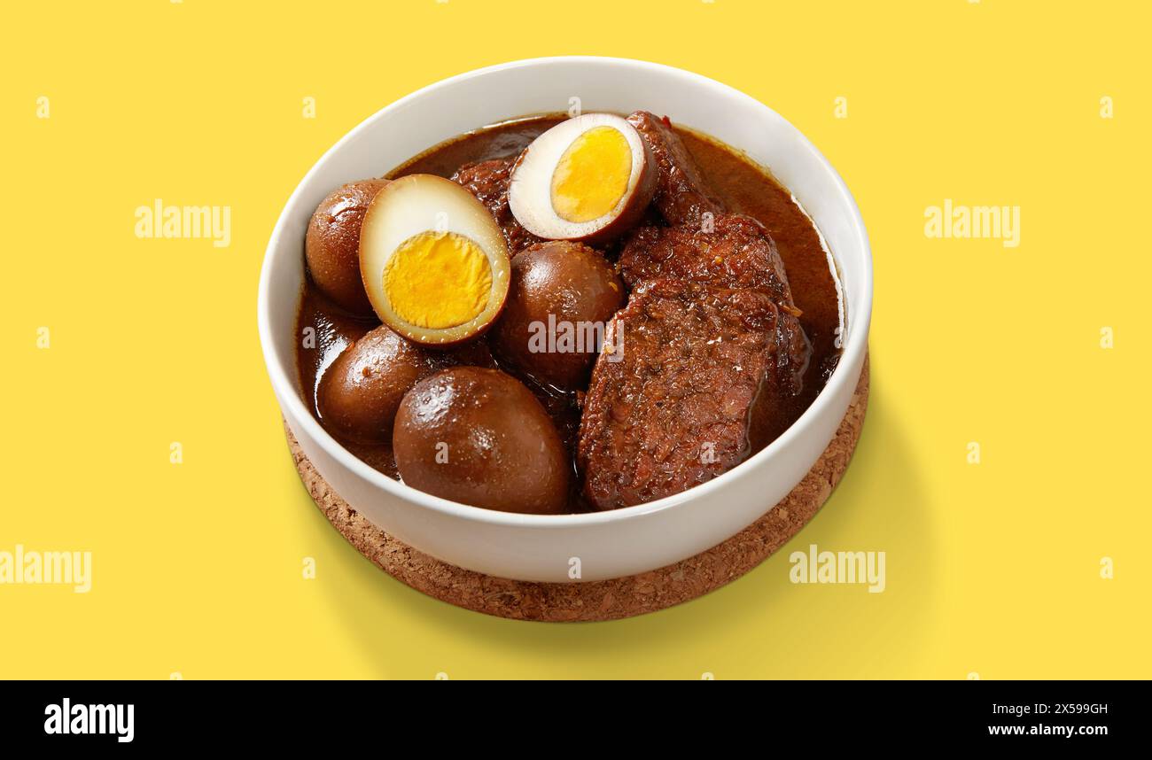 A bowl of delicious boiled egg and tempeh stew with yellow background ...