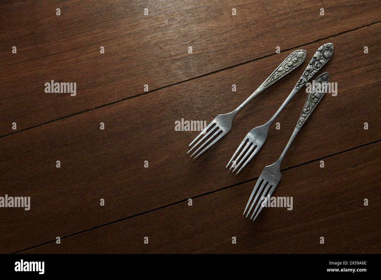 Three old silver forks with ornate carvings on the handles on a wooden ...