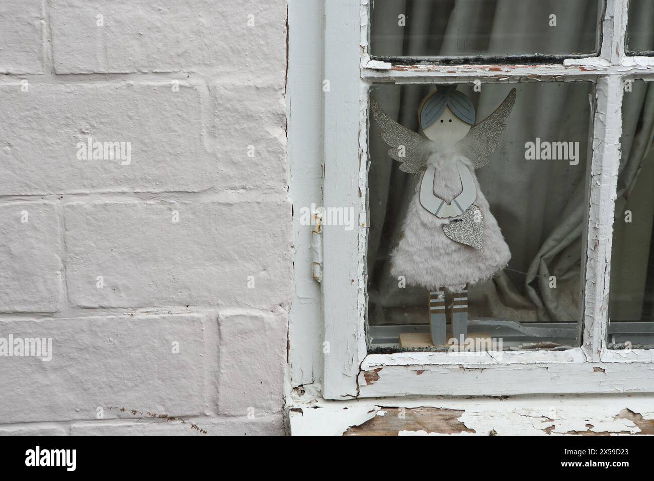 Toy angel in looking out of window of house peeling paint on window ...