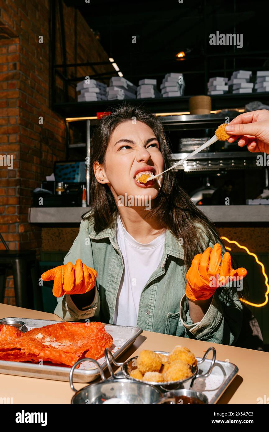 A female diner bites into a skewered crispy chicken wing while being ...