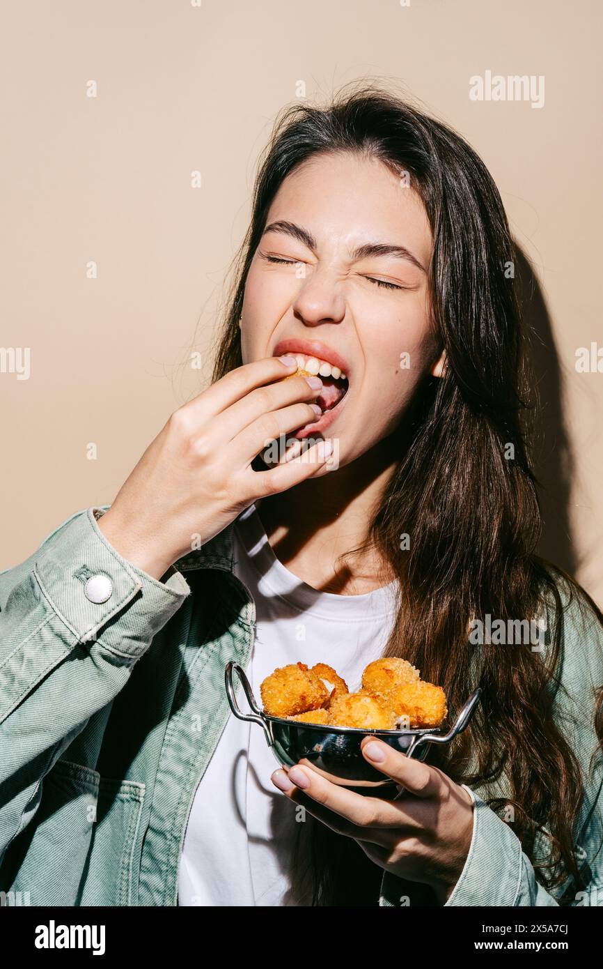 A cheerful young woman in a casual outfit biting into a golden fried ...
