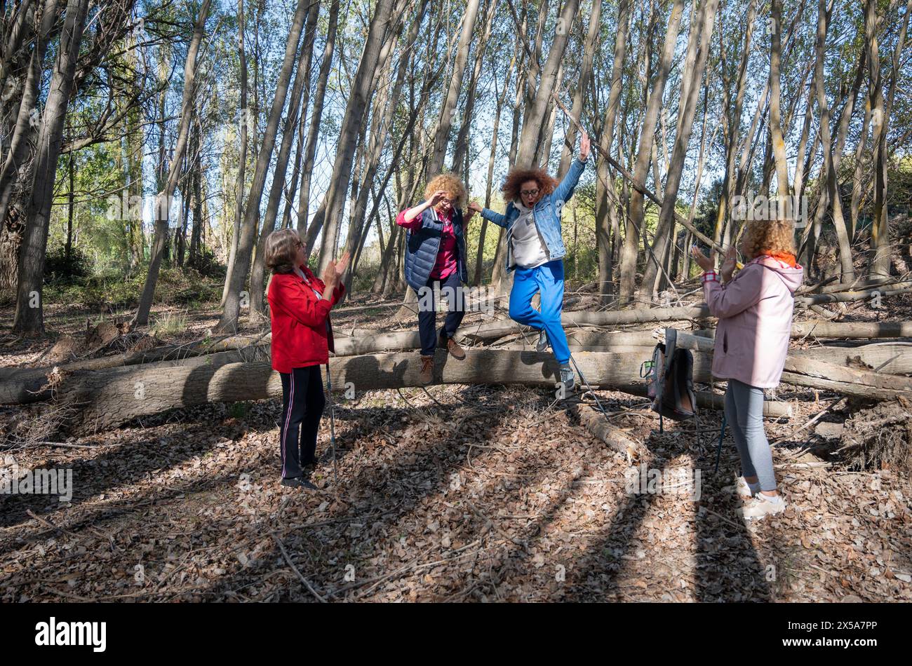 A group of cheerful friends captures memories, jumping over a log in a ...