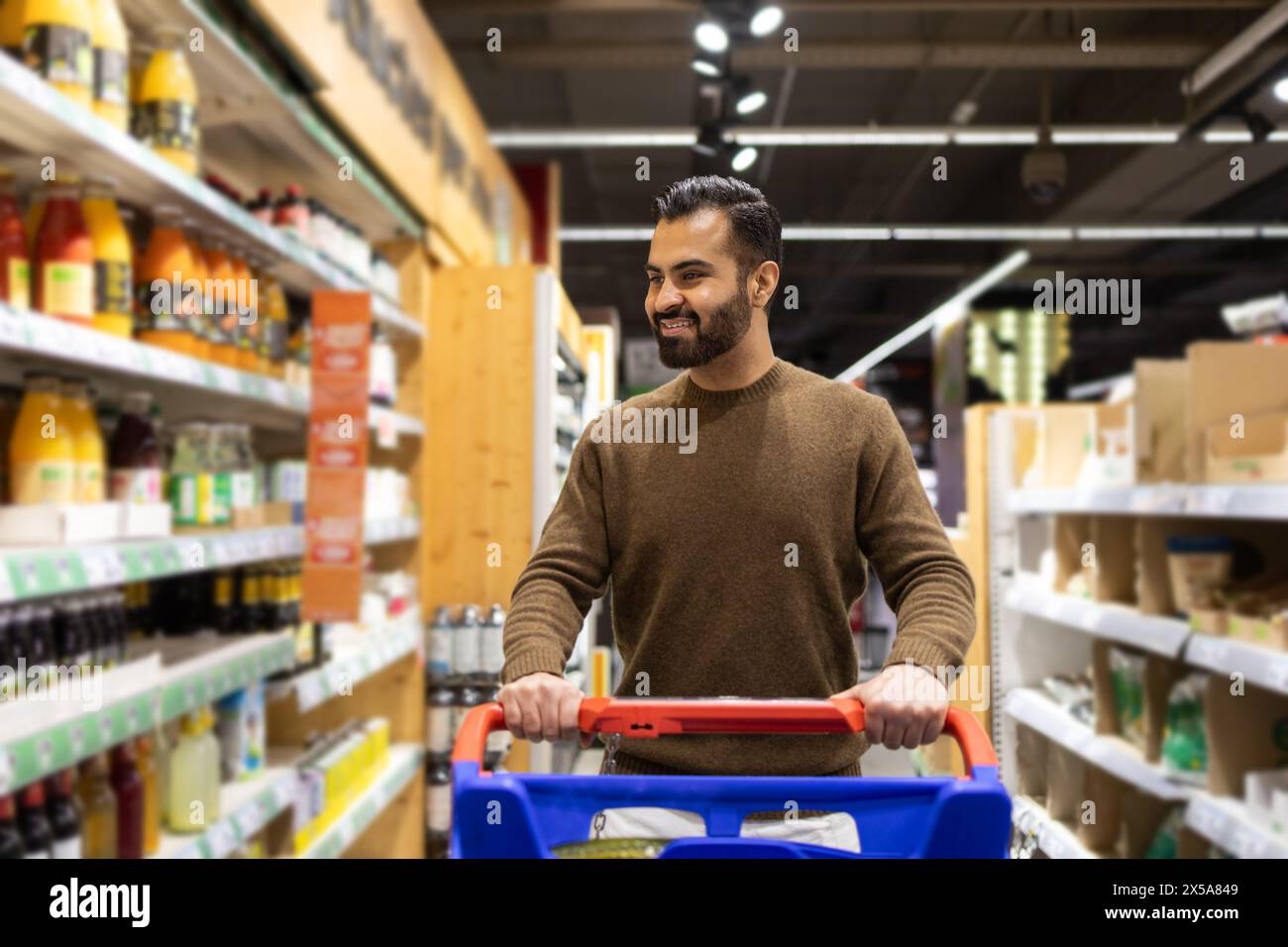 Happy male shopper pushing a blue cart down the aisle of a well-stocked ...