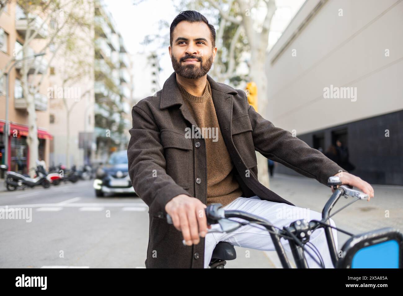Stylish man with a beard enjoying a bike ride through the city streets ...
