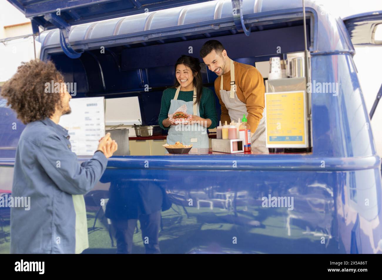 Cheerful friends serve a happy customer from their vibrant blue food ...