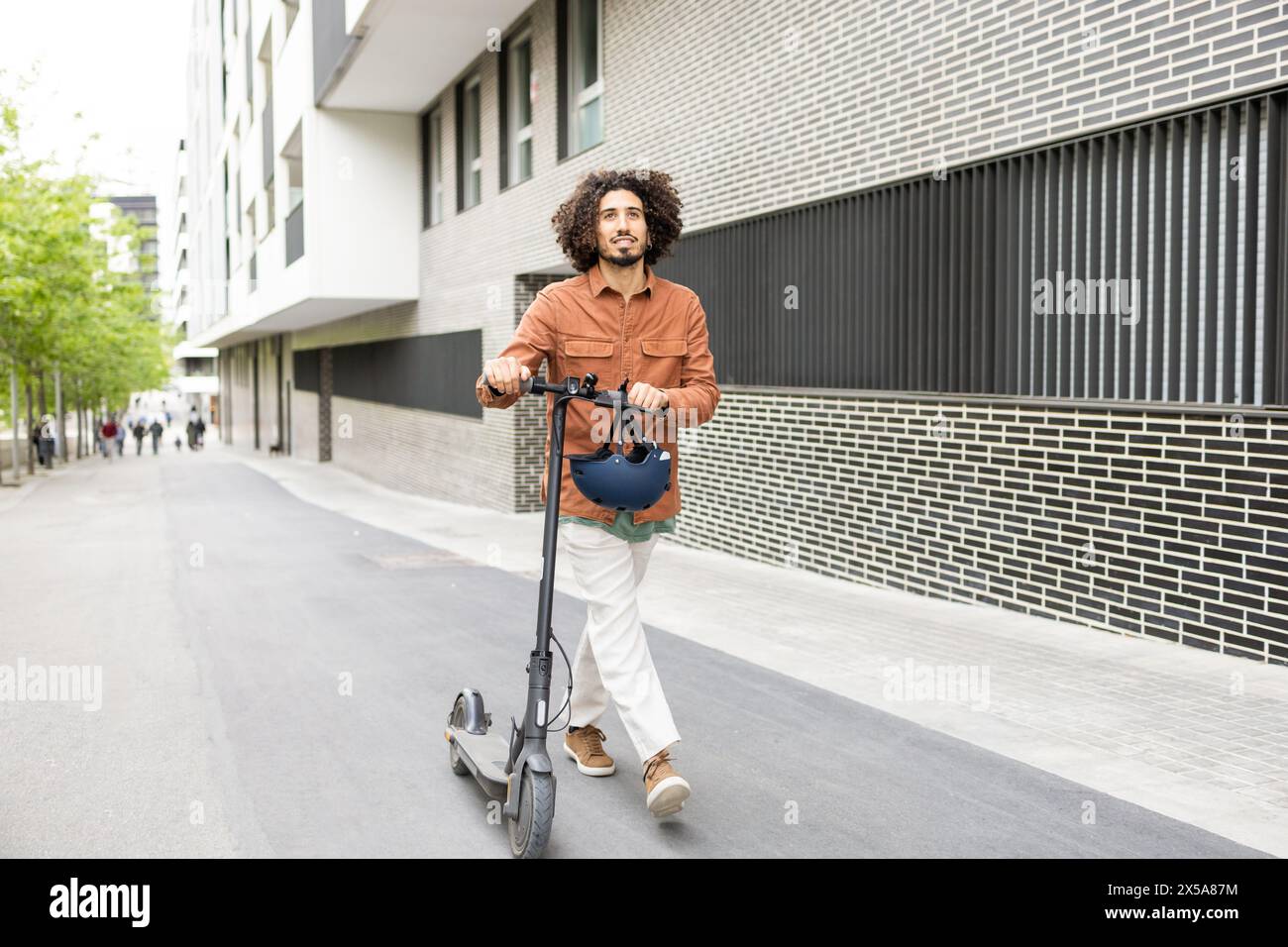 A stylish young man with curly hair rides an electric scooter on a city ...
