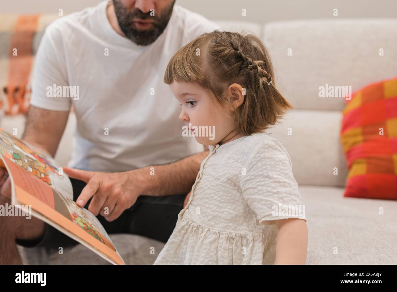 A father reads a book to his young daughter, showing a moment of family ...