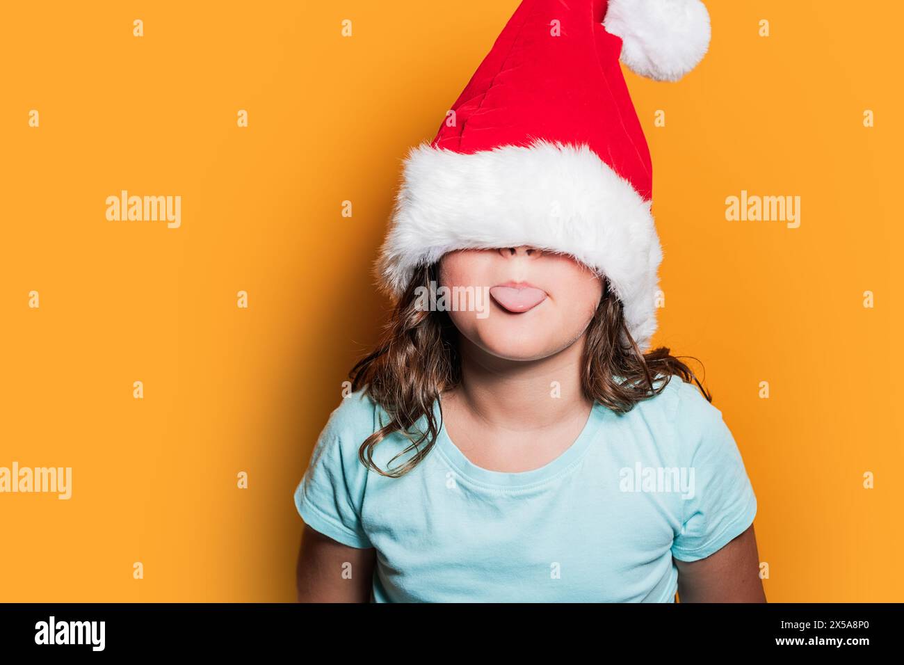 Anonymous child wearing a red Santa hat playfully sticks out their ...