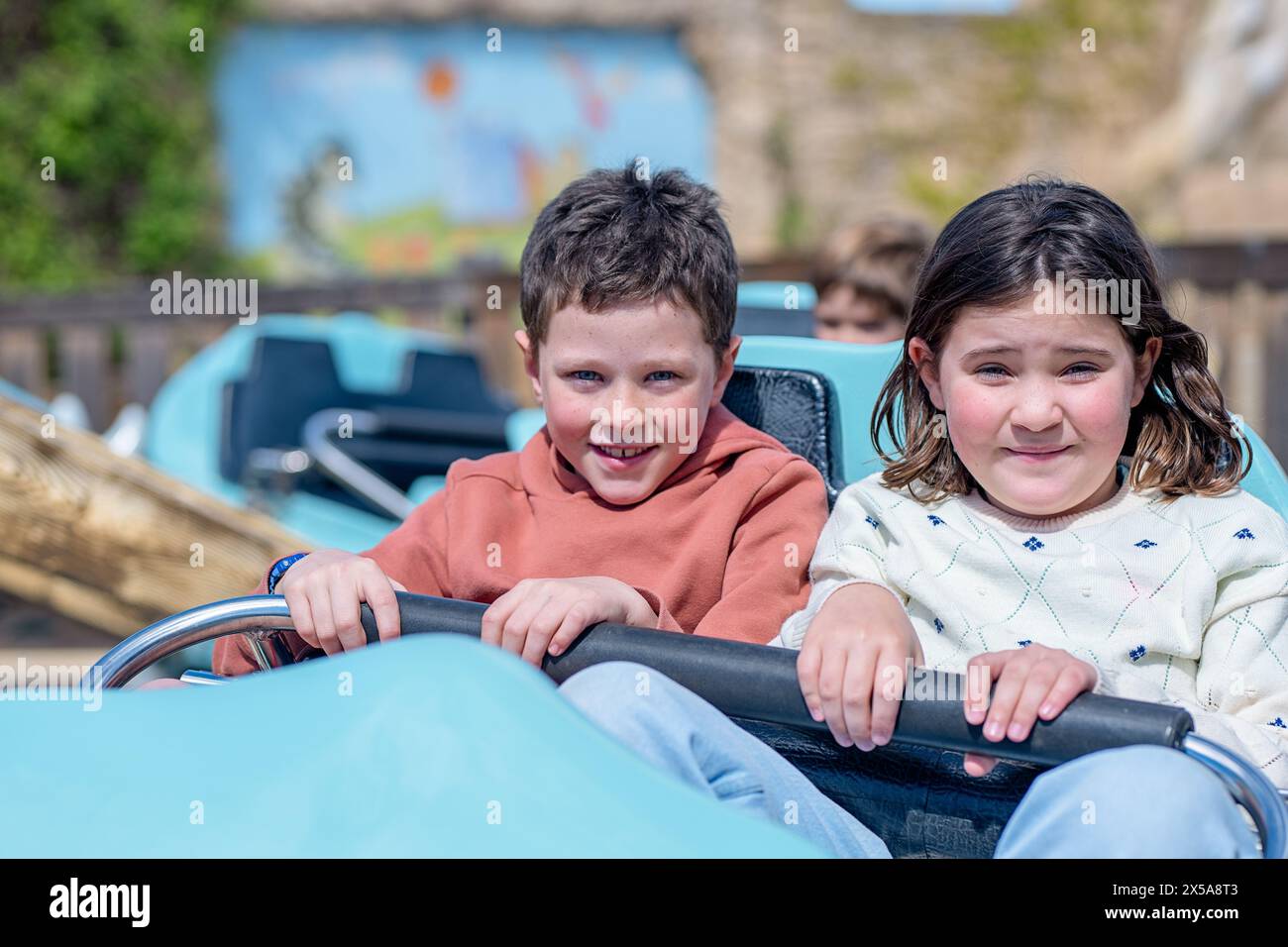Two joyful kids, a boy and a girl, enjoying a thrilling rollercoaster ...