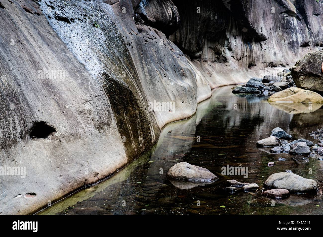 A serene riverbed flanked by smooth, worn rocks in the shadows of a ...