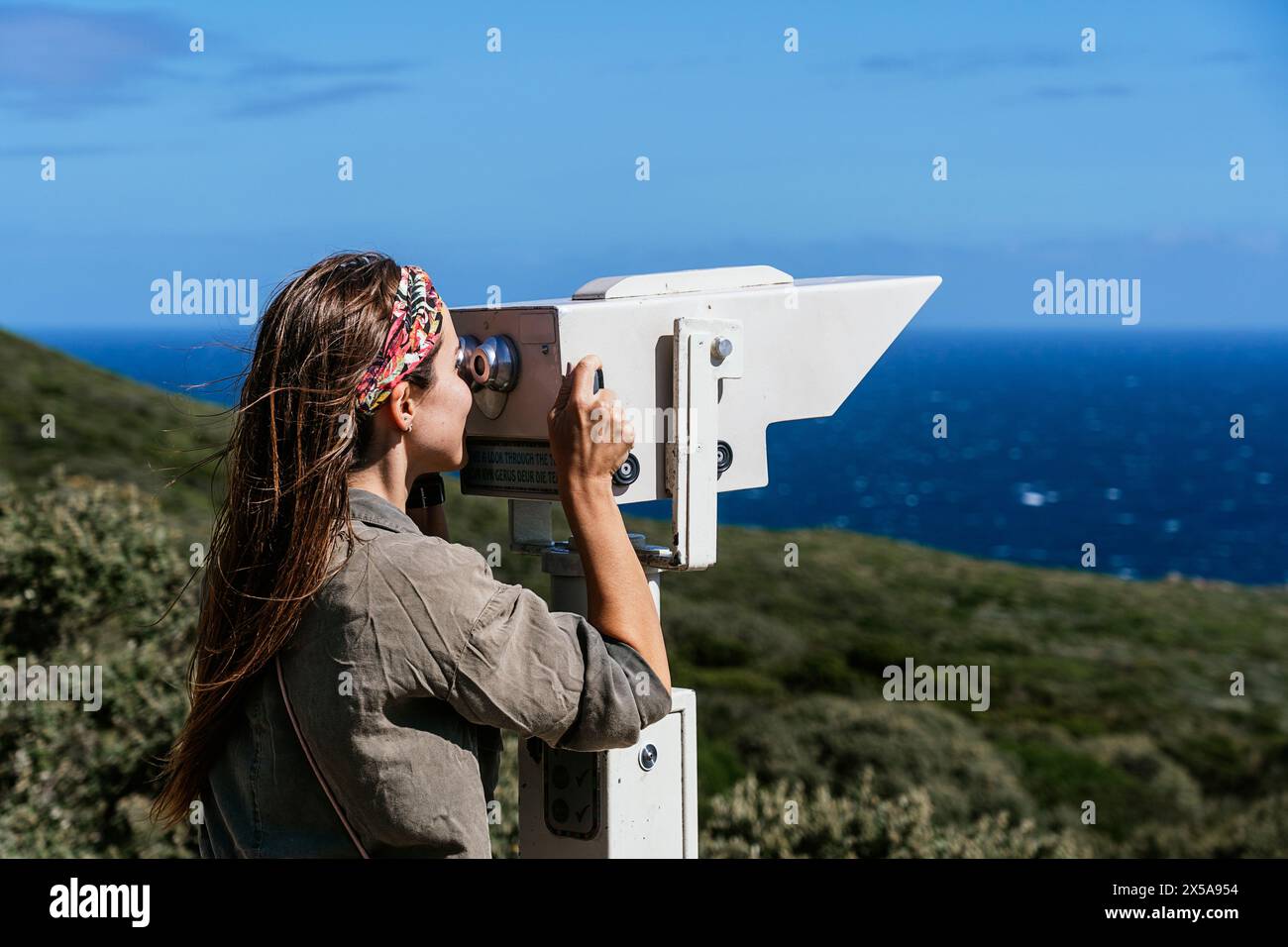 A young female tourist is using a coin-operated viewing scope to ...