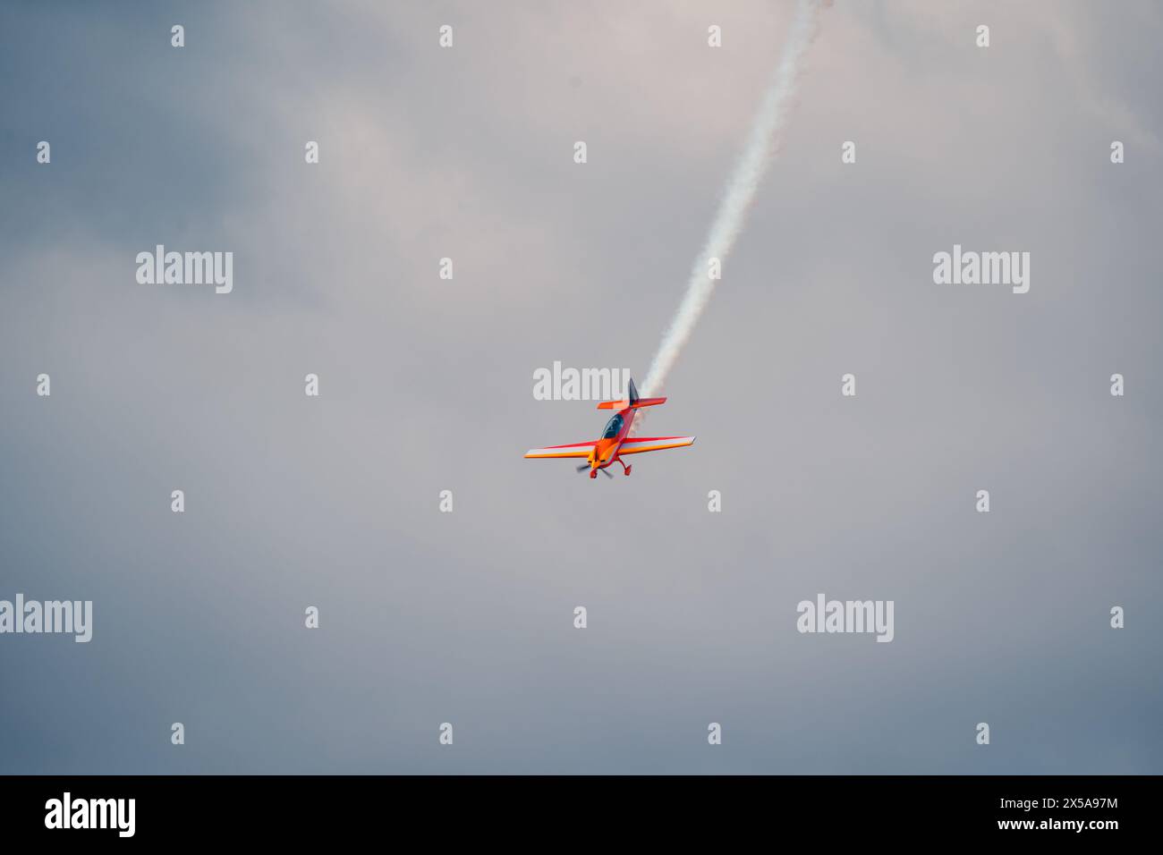 From below, a stunt plane with vivid orange and blue colors soars in ...