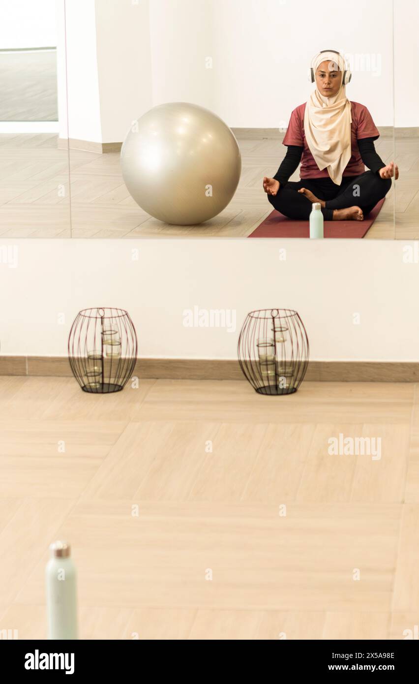 A Muslim woman in a hijab seated in a meditative pose in a locker room ...
