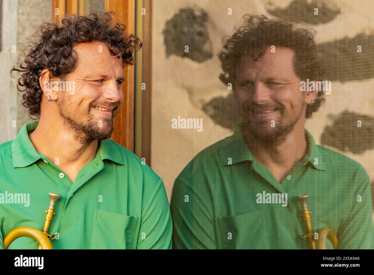 A one-armed man with curly hair smiles while holding a trumpet ...