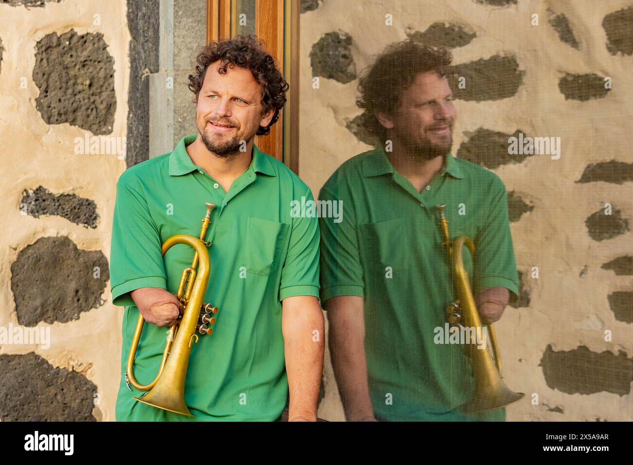 An inspiring one-armed street trumpeter in a green shirt, looking away ...