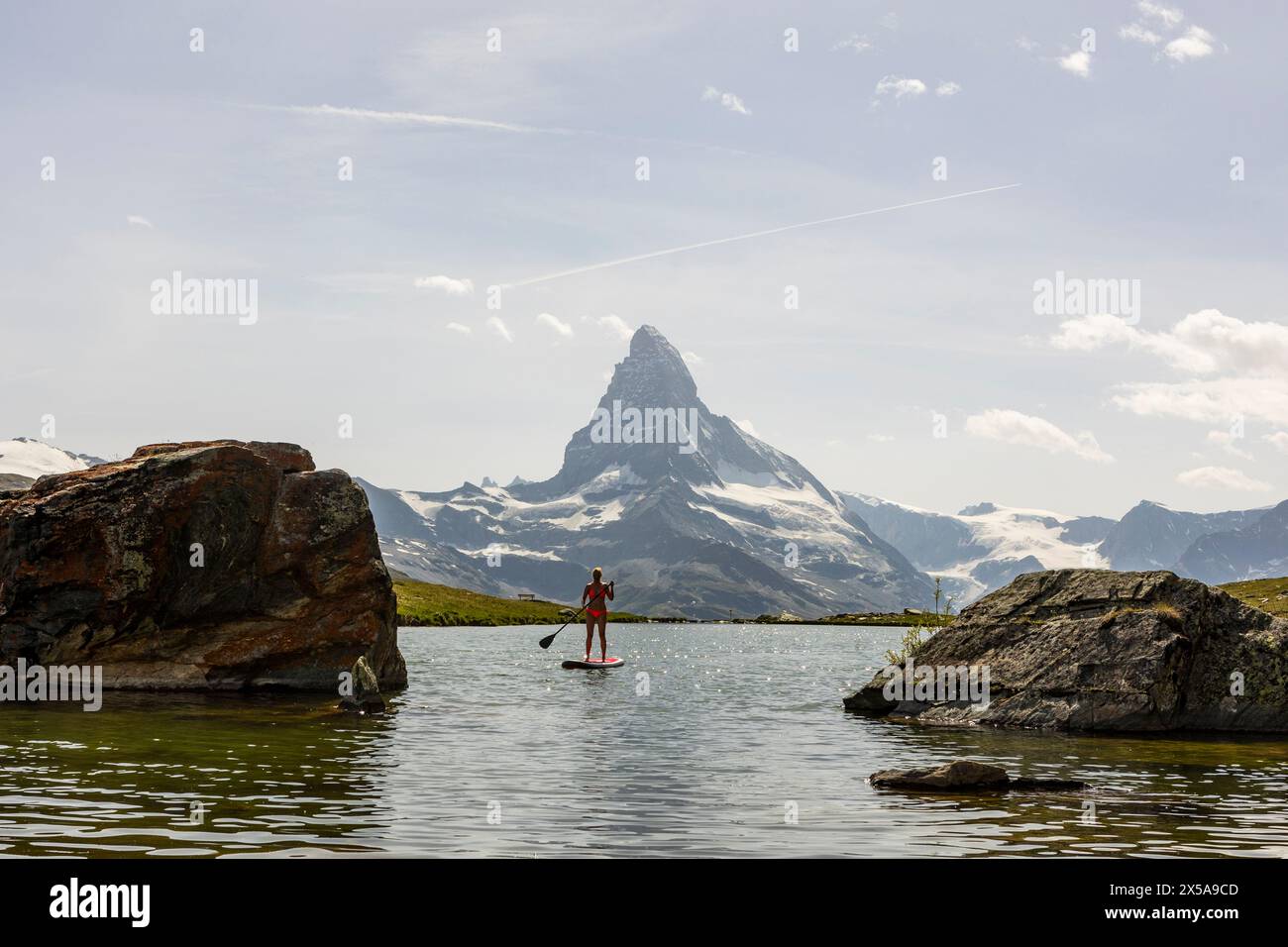 A woman paddle surfing on a tranquil mountain lake, with the iconic ...