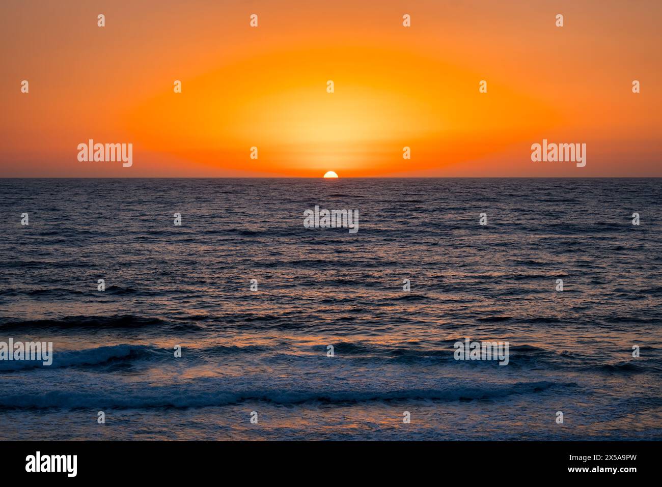 Captivating sunset over the tranquil sea in Sardinia, with warm orange hues and the sun ...