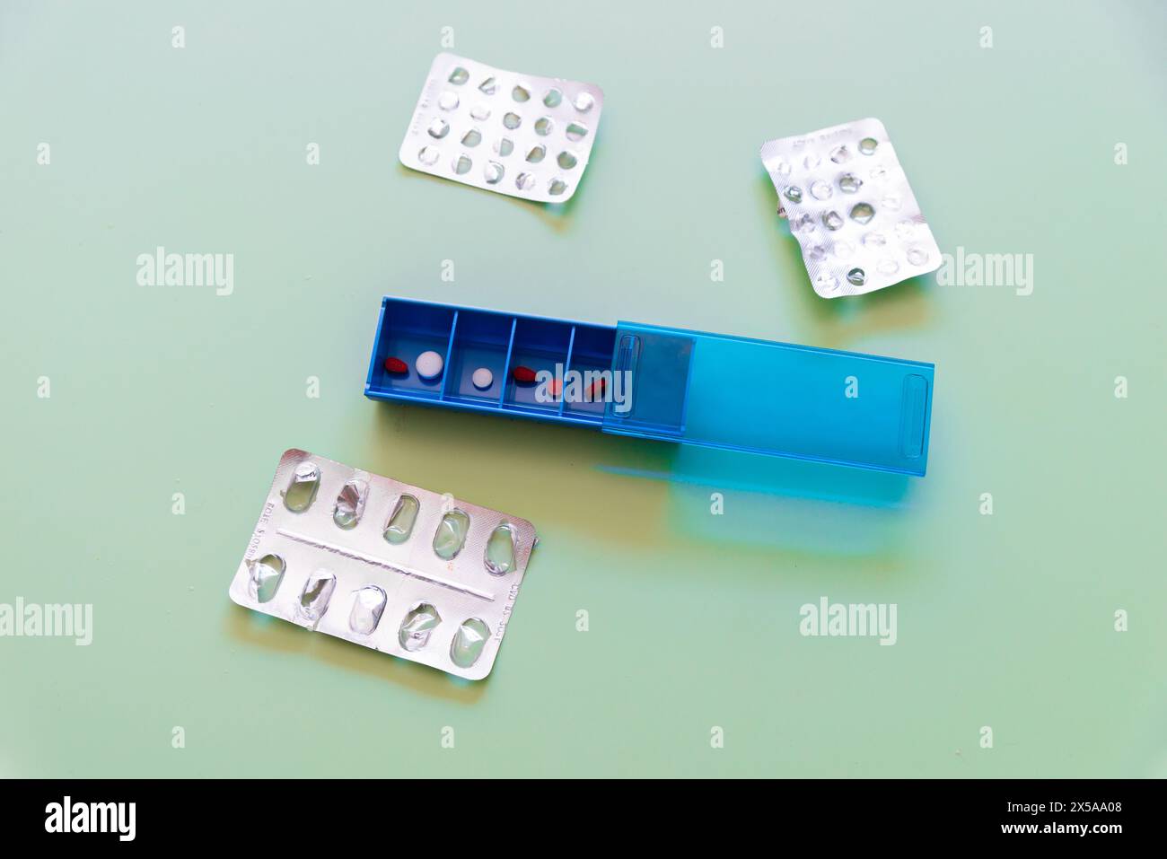 A blue day pill box with assorted pills alongside empty blister packs ...
