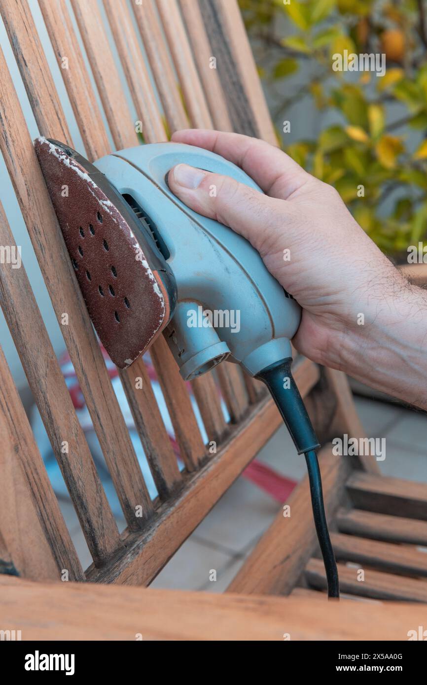 A close-up of a man's hand using an electric sander to smooth and ...