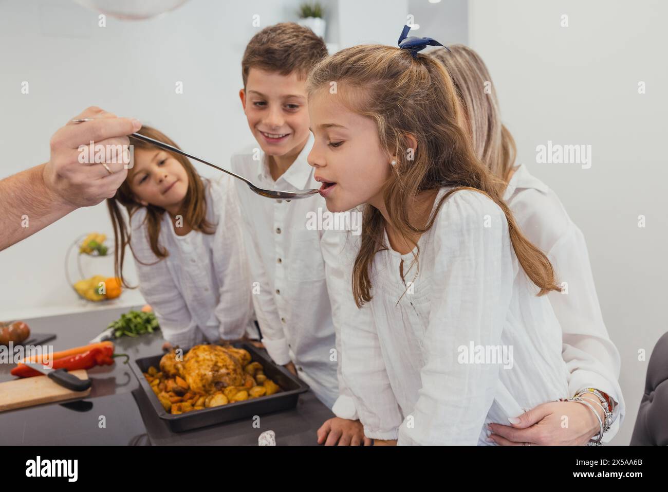 A joyful family participates in cooking a roast chicken with fresh ...