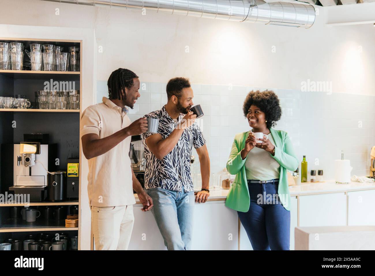 Three colleagues enjoy a coffee break, chatting in a modern coworking ...