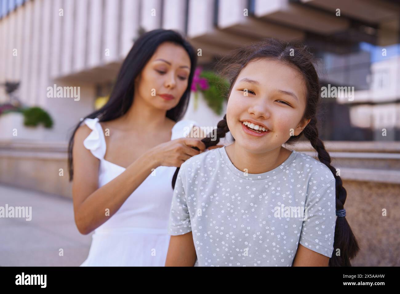 A smiling girl on the autism spectrum, looks on while her mother ...