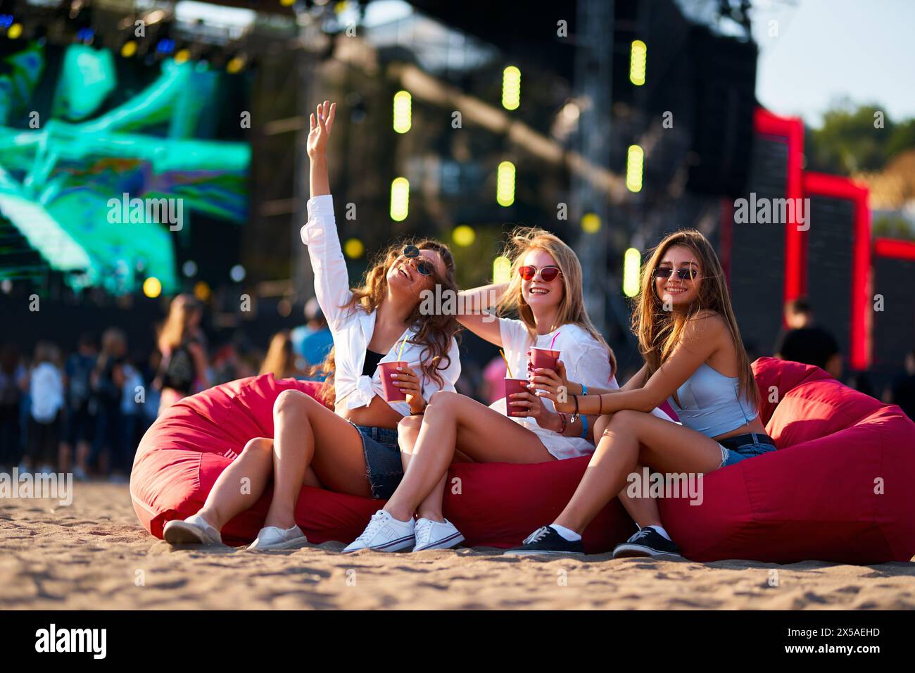 Three women sit on red bean bag chairs at beach music festival ...