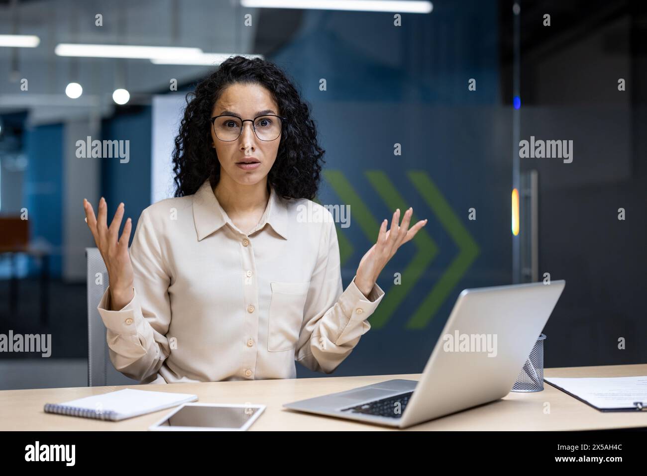 In a modern office setting, a Hispanic businesswoman displays confusion ...