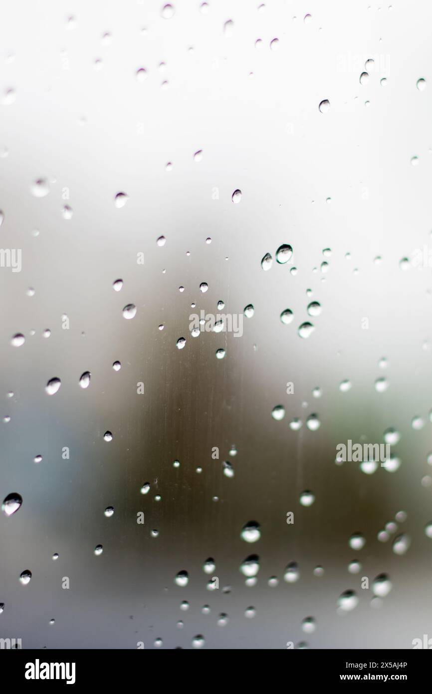 Water droplets cascade down a glass window, creating a blurry backdrop ...