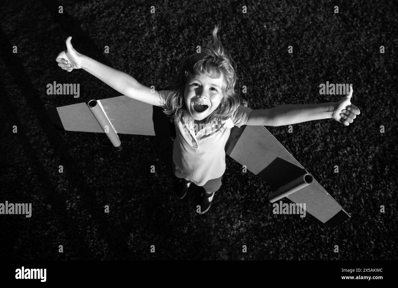 Excited funny child boy flying in plane made craft of cardboard wings ...