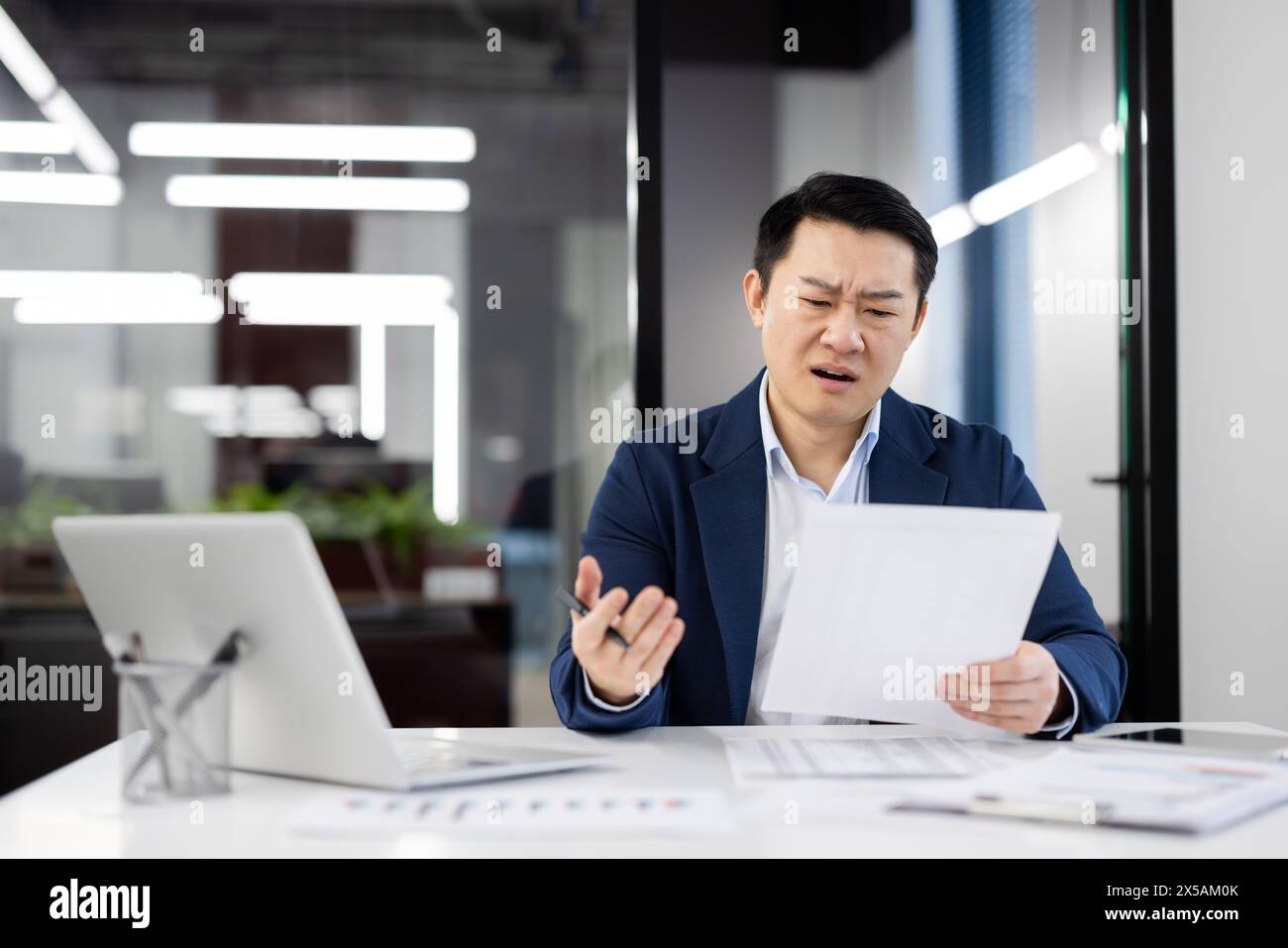 A businessman looks perplexed while examining documents at his work ...