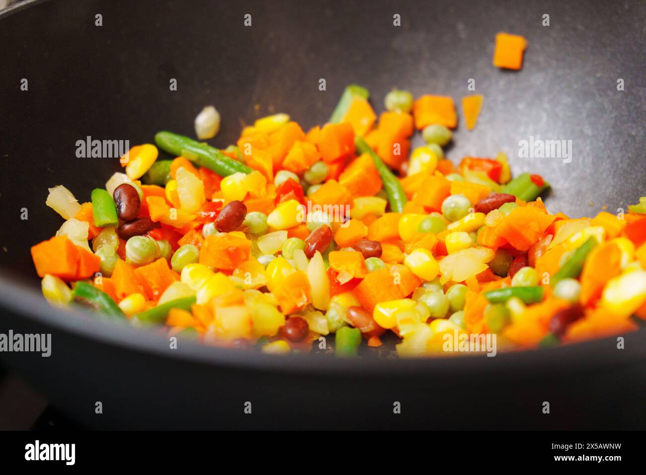 Colorful chopped vegetables is being stirred using a wooden spoon. The ...