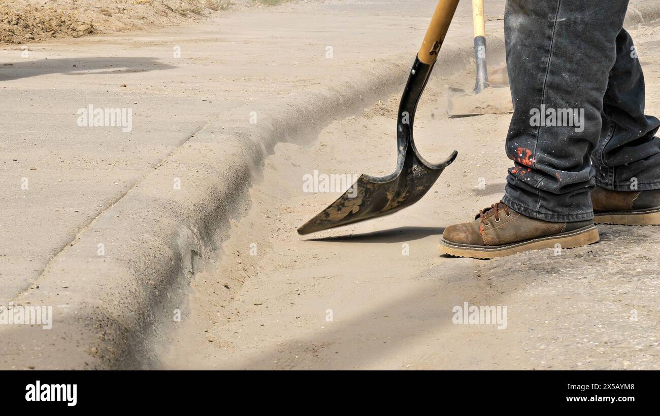 Construction workers use a shovel to clean dirt off the street next to ...
