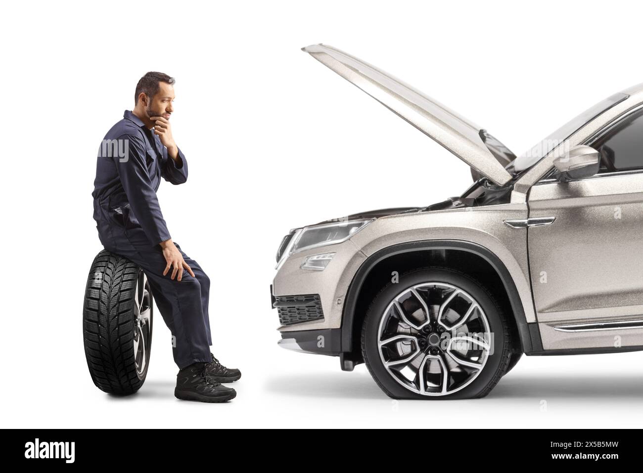 Car mechanic in a uniform sitting on a tire in front of a SUV and ...