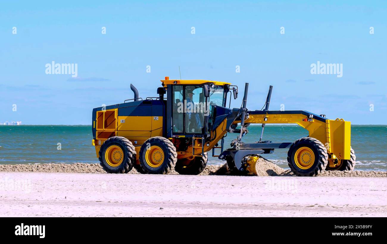 Yellow road grader levels the sand on the beach at the Gulf of Mexico ...