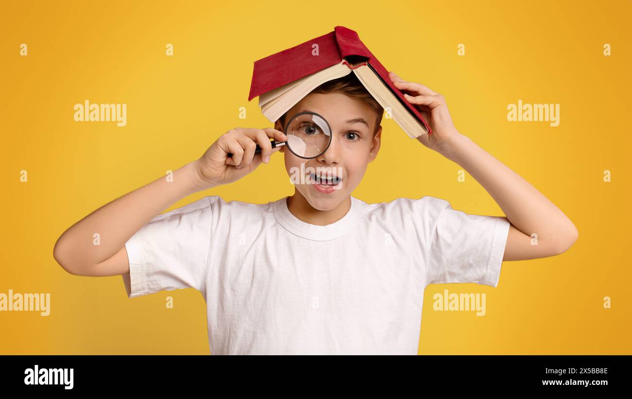 Cute clever boy with magnifying glass in hand hiding under book Stock ...