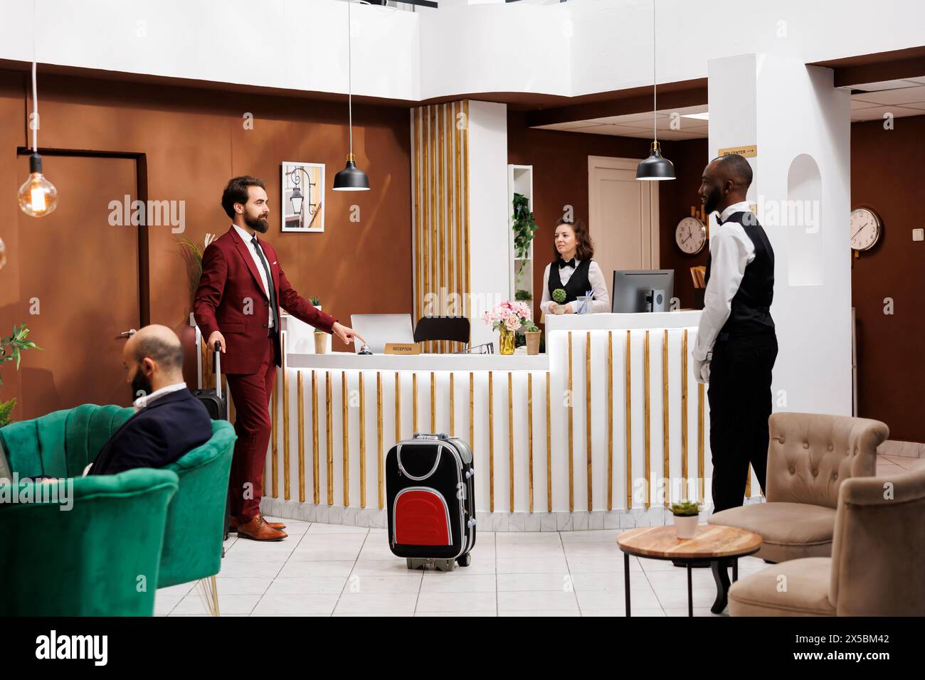White collar worker welcomed by hotel staff at reception, carrying ...