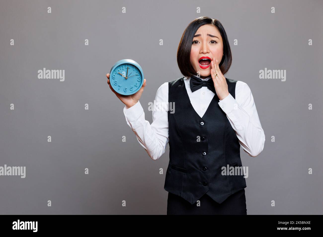 Anxious asian waitress panicking while holding circle dial alarm clock ...