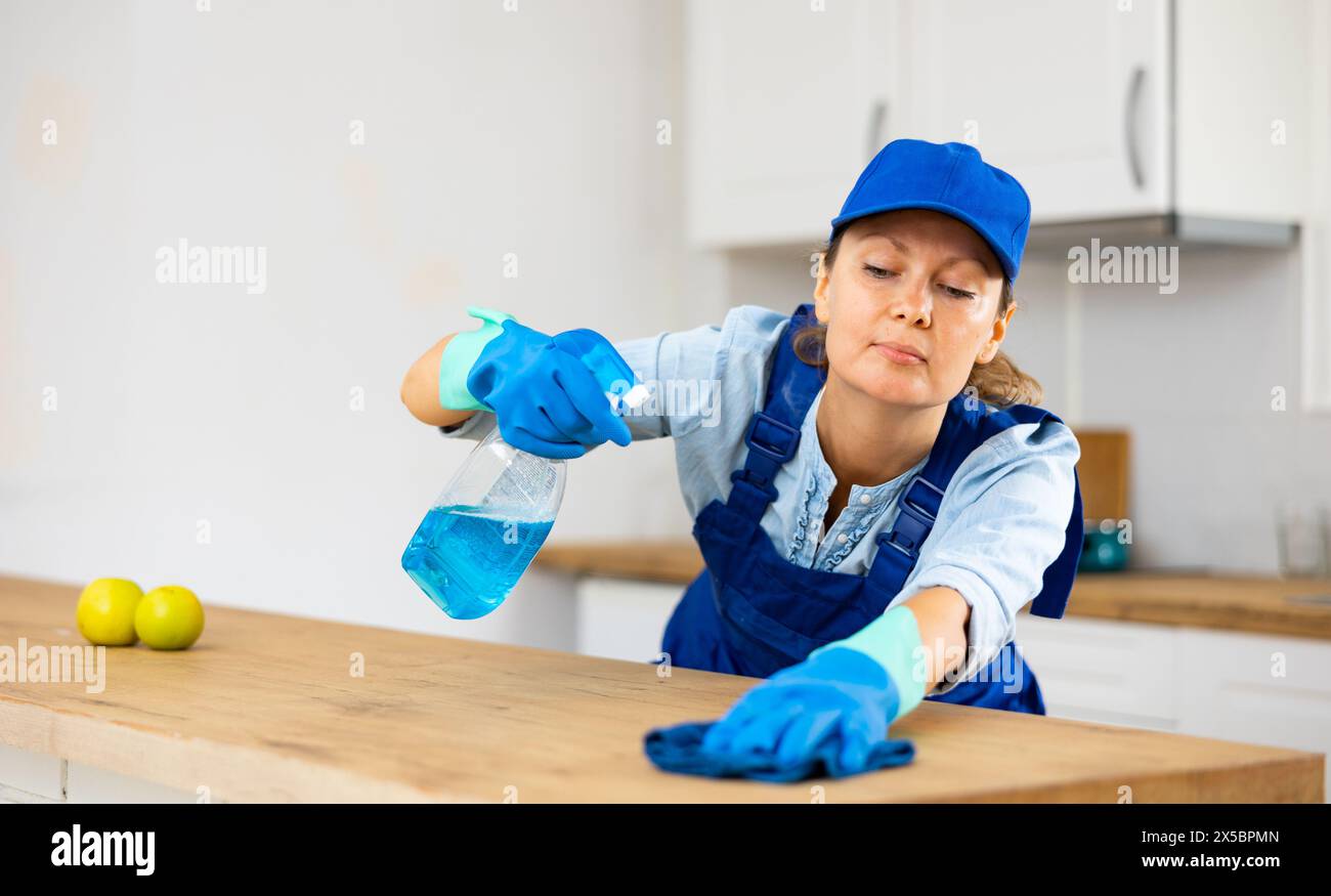 Skilled woman house cleaner sanitizing kitchen countertop Stock Photo ...