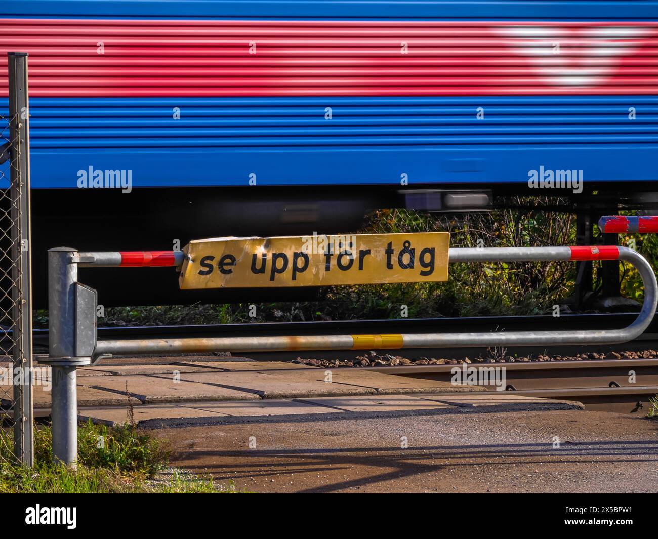 Swedish train passing a railway crossing with a warning sign saying ...