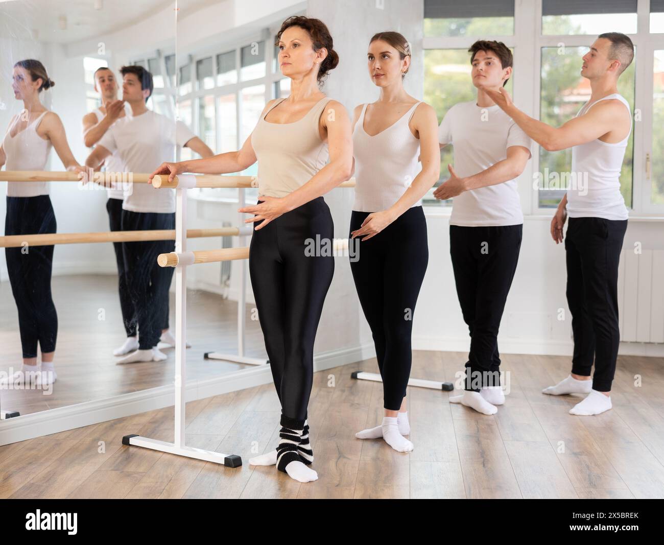 Ballet students practicing basic positions at barre with instructor ...
