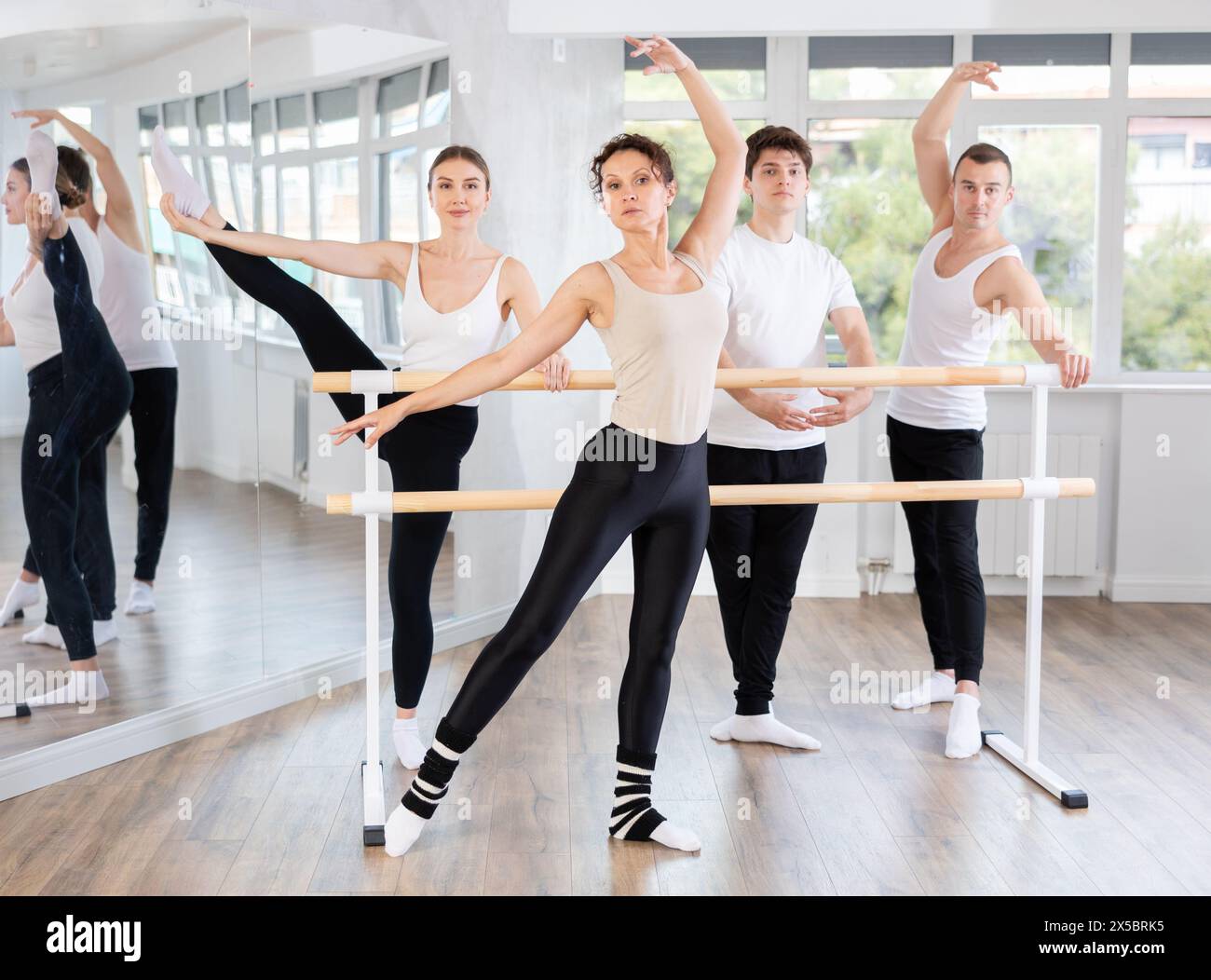Group of people doing ballet exercises and posing using barre in gym in ...