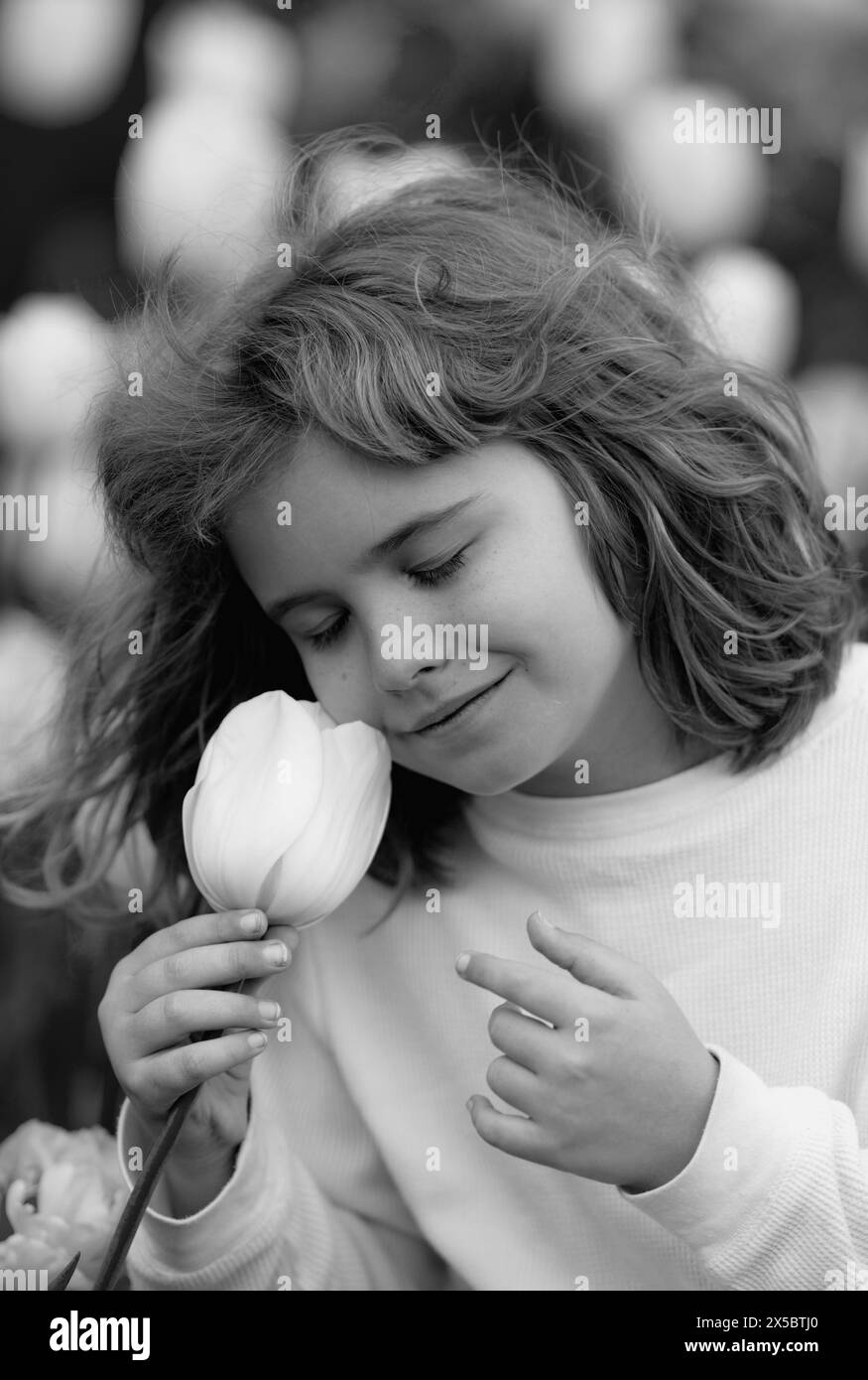Cute pretty blonde kid with eyes closed smelling tulip flower in the ...