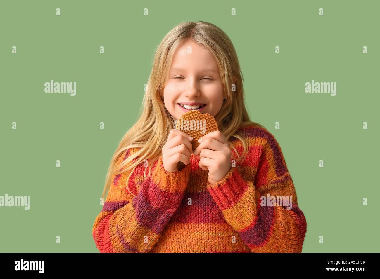 Cute little girl eating waffle on green background Stock Photo - Alamy