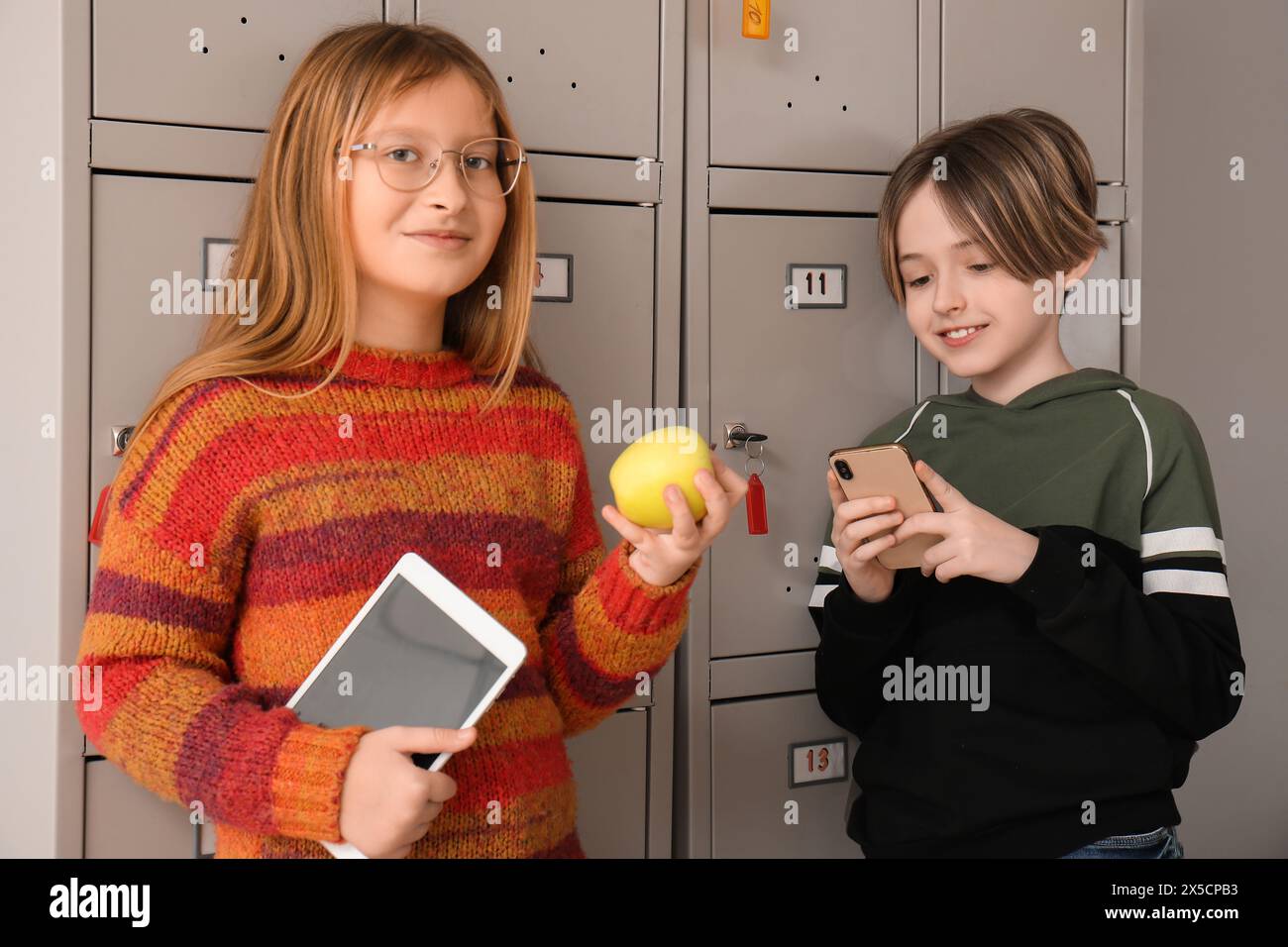 Cute little pupils with gadgets and apple near locker at school Stock ...