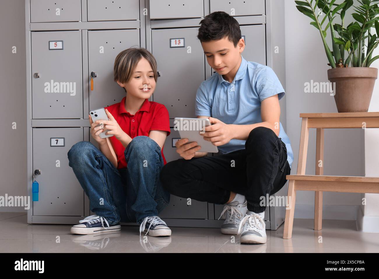 Little schoolboys using gadgets near locker at school Stock Photo - Alamy