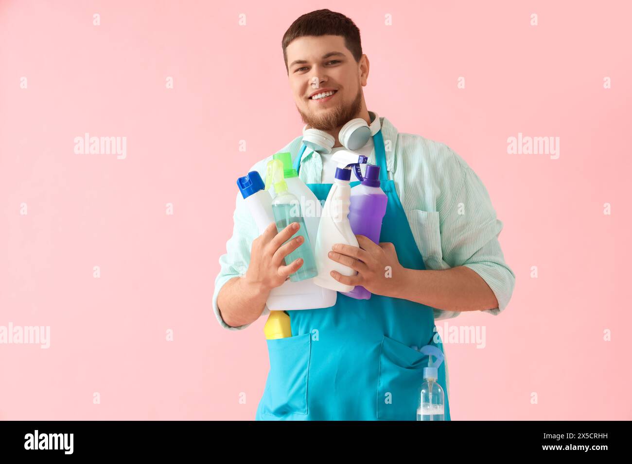 Male janitor with bottles of detergent on pink background Stock Photo ...