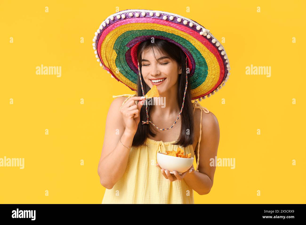 Young woman in sombrero with eating nachos on yellow background. Cinco ...